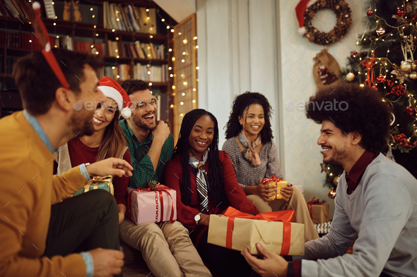 Cheerful friends having fun while giving each other Christmas presents at home. Stock Photo by ...